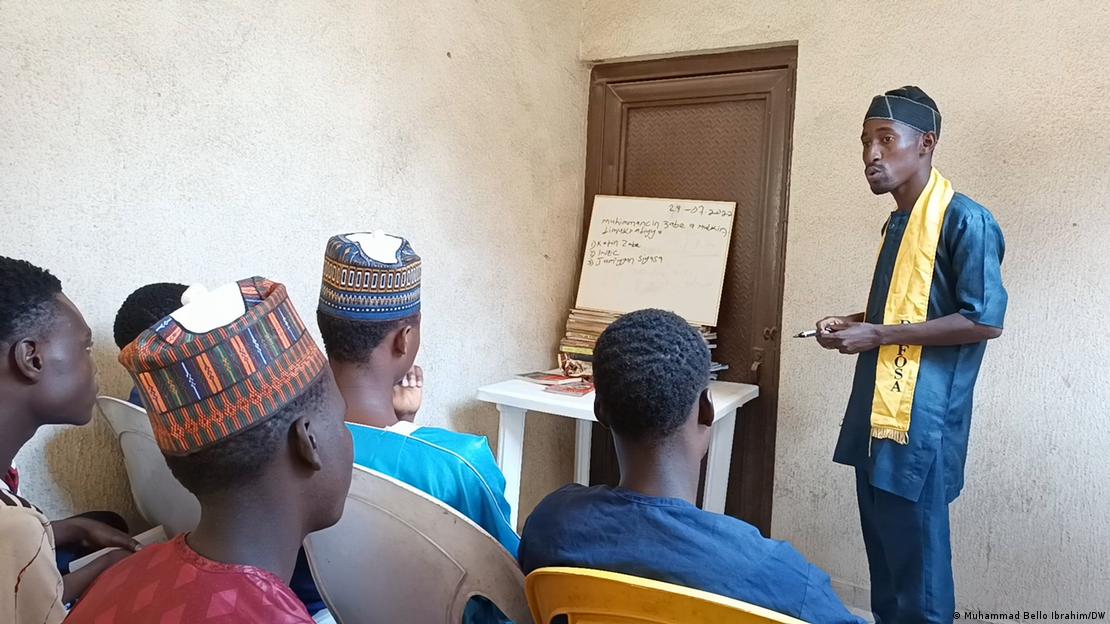 A young Nigerian stands in front of a group listening to him